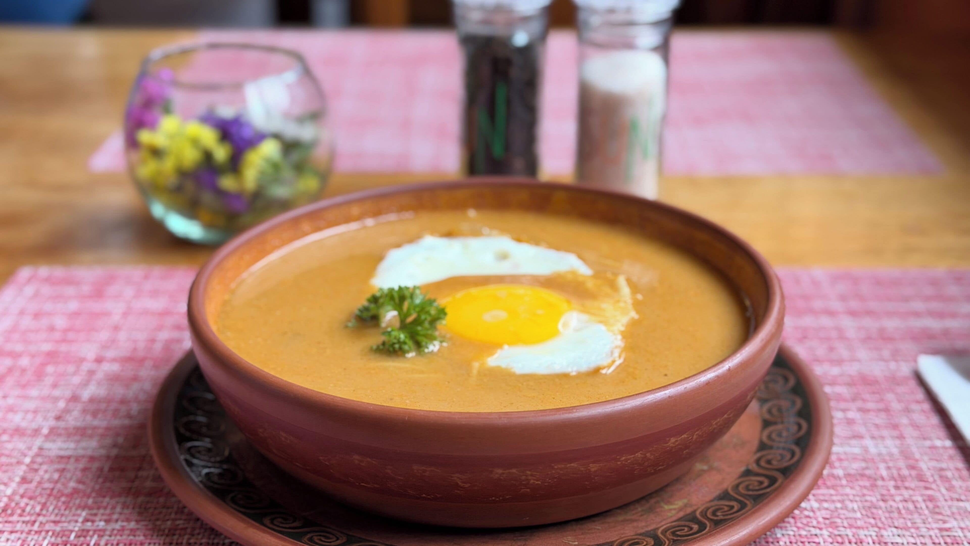 Uma tigela de sopa com um ovo por cima, colocada em um prato estampado.