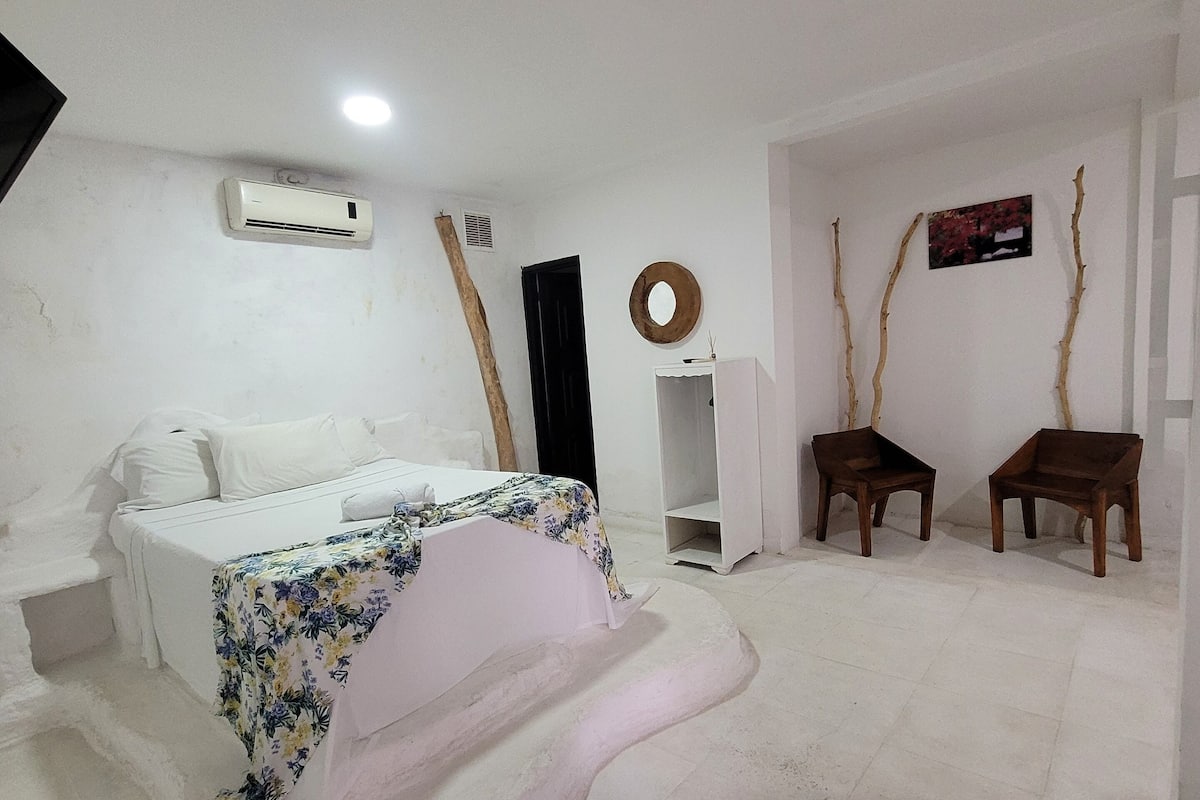 Quarto com cama, guarda-roupa, uma mesinha e ar-condicionado fixado na parede.