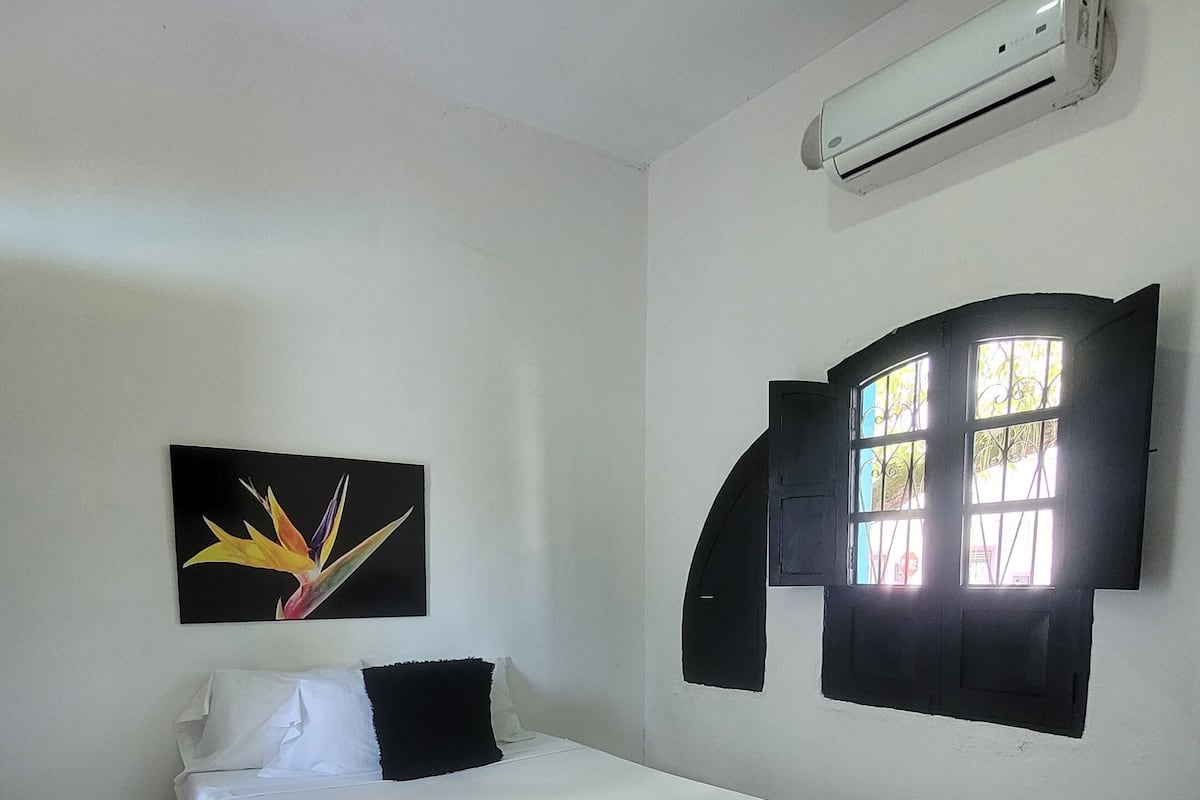 Quarto de hotel com cama, um banquinho, televisão fixada na parede, ar condicionado e uma janela com vista.