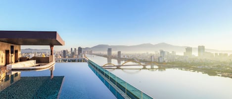 Piscina infinita no terraço com vista para a paisagem urbana, uma ponte e uma cordilheira ao longe.