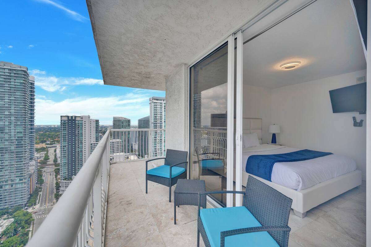 Uma varanda com cama, televisão e vista para edifícios altos.