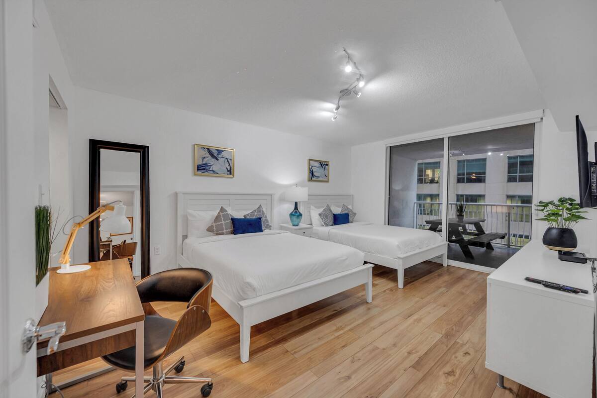 Quarto moderno com duas camas, uma escrivaninha e varanda com vista.
