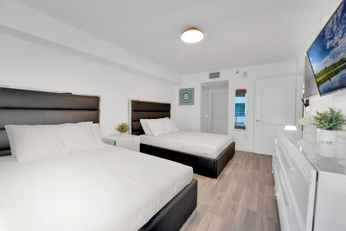 Quarto de hotel moderno com duas camas, televisão de tela plana e vista para o exterior.