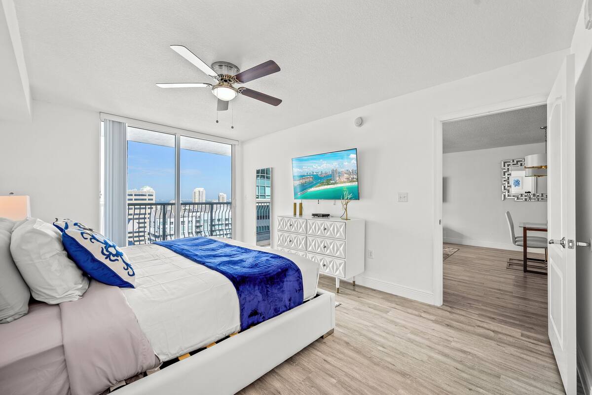 Quarto moderno com cama, ventilador de teto, televisão e vista para a cidade.