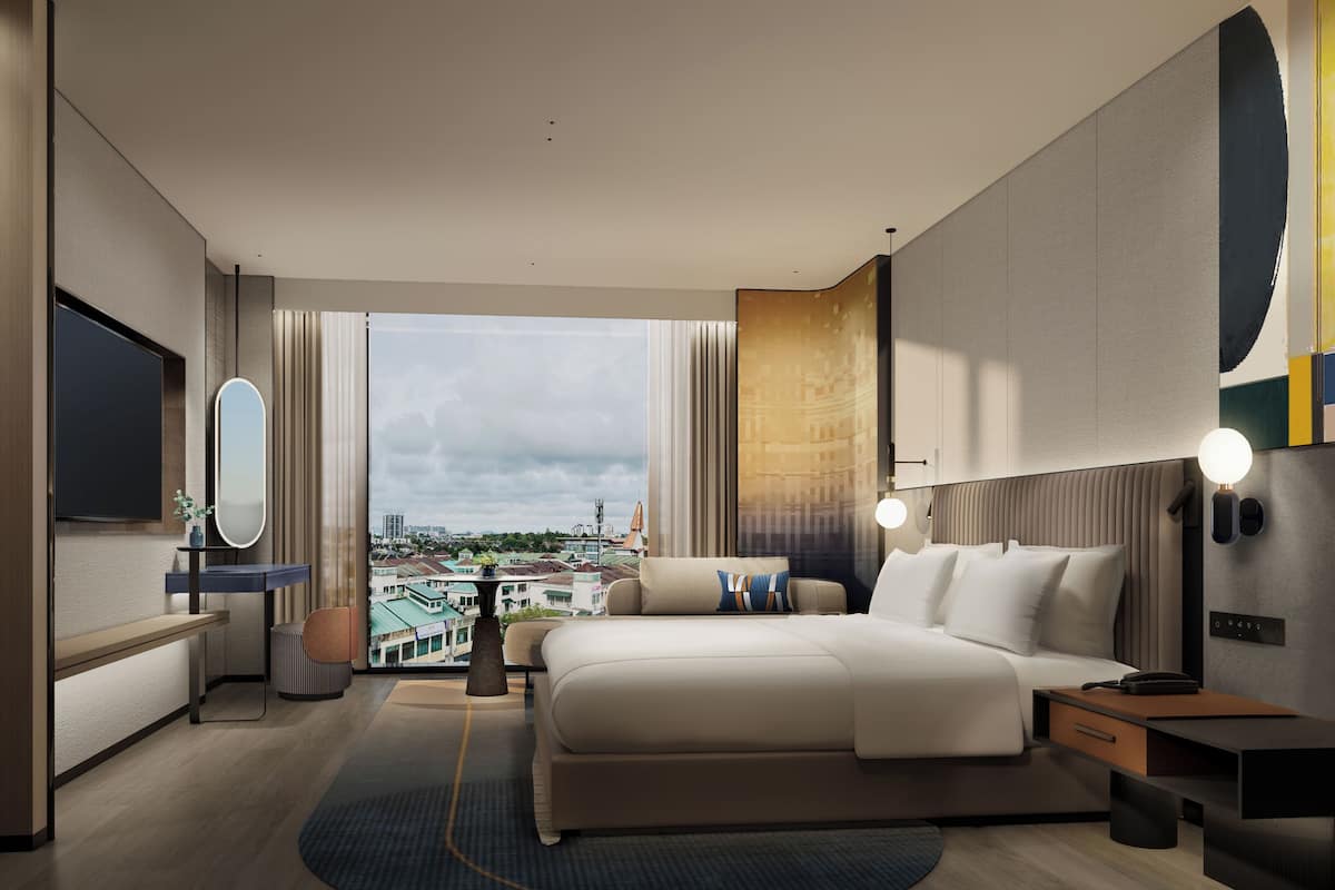 Quarto de hotel moderno com uma cama grande, mesas de cabeceira, escrivaninha e uma ampla janela com vista para a cidade.