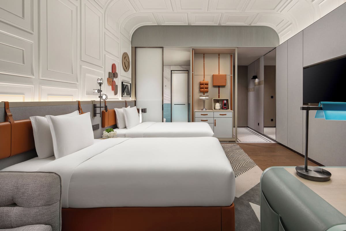 Quarto de hotel com cama grande, mesas de cabeceira, escrivaninha, televisão e banheiro visível por uma porta aberta.
