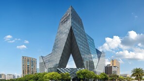 Um hotel moderno com um design angular característico, rodeado por outros edifícios e árvores.