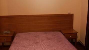 Quarto com cama, mesa de cabeceira, ar condicionado e luminária fixa na parede.