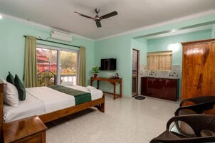 Quarto com cama, escrivaninha, televisão, guarda-roupa e ventoinha no teto.