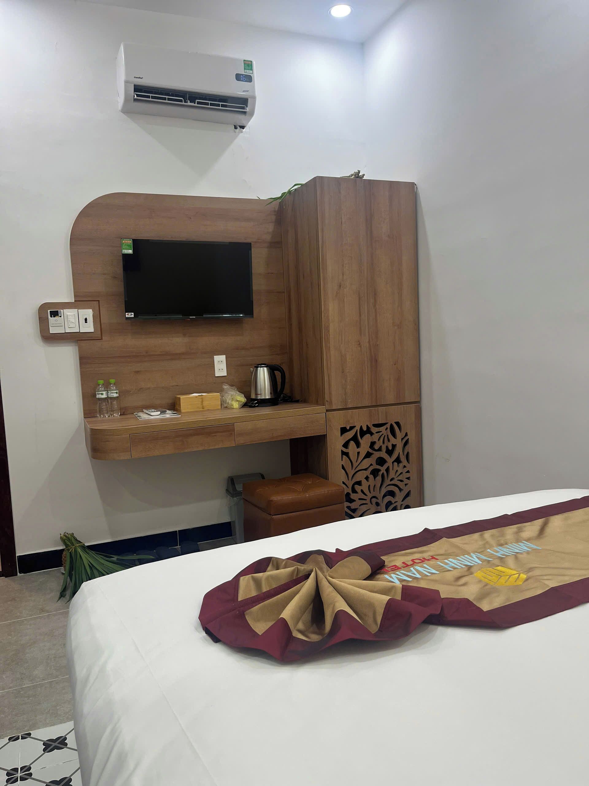 Quarto de hotel com escrivaninha de madeira, televisão de tela plana, minibar, máquina de café e cama com manta decorativa.