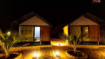 Duas cabanas de madeira com janelas e portas amplas, cercadas por jardins bem cuidados e caminhos.