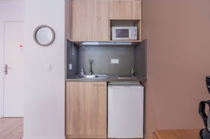 Uma cozinha compacta equipada com micro-ondas, pia e lava-louças, armários de madeira e um espelho redondo.