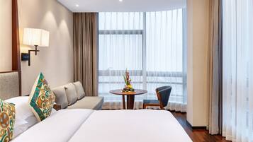 Quarto de hotel com uma cama grande, um sofá, uma mesa pequena com um vaso e uma cadeira.