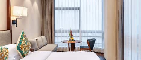 Quarto de hotel com uma cama grande, um sofá, uma mesa pequena com um vaso e uma cadeira.