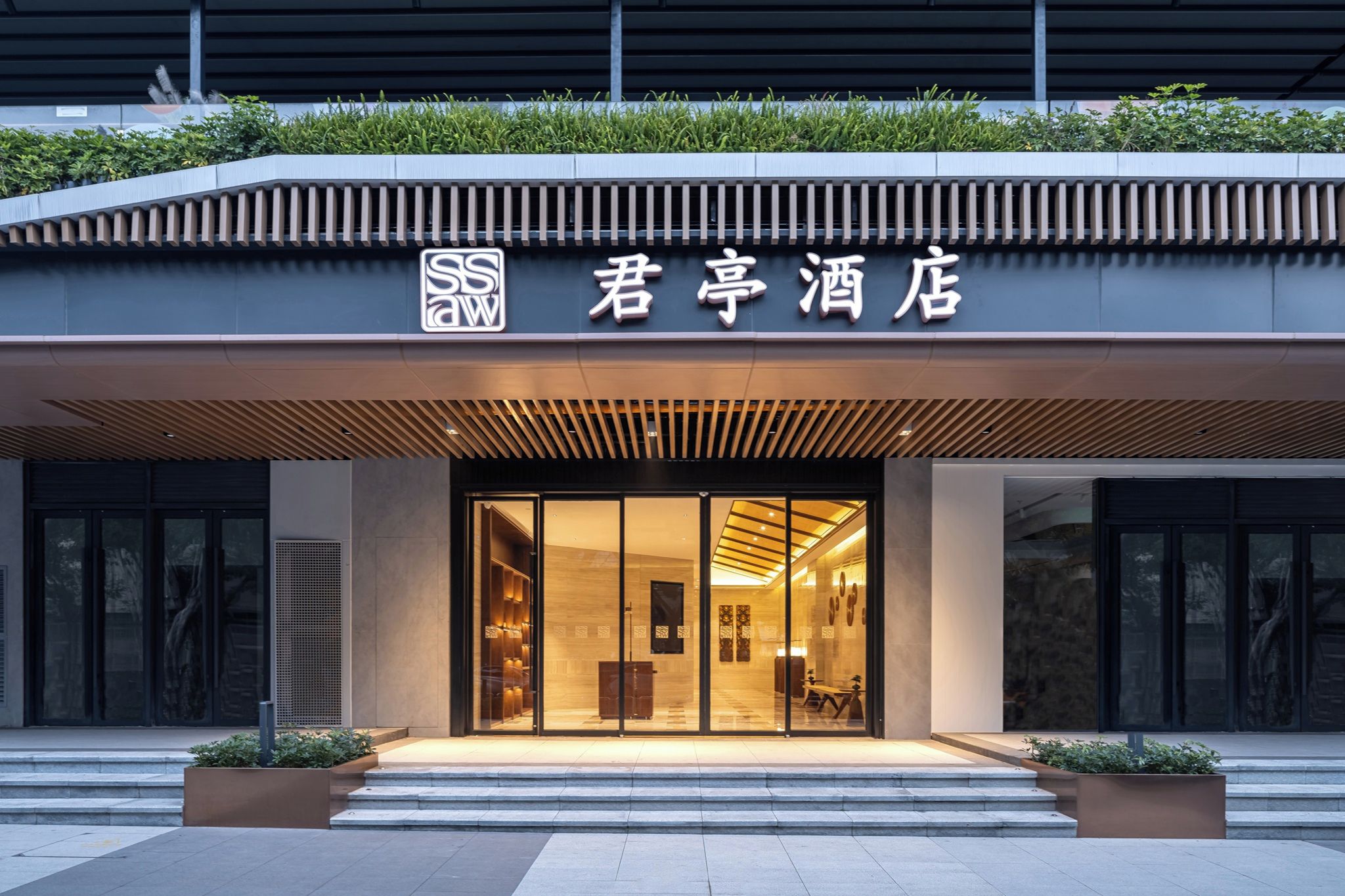 Entrada de hotel com design moderno, destacando uma placa e interior bem iluminado visível pelas portas de vidro.