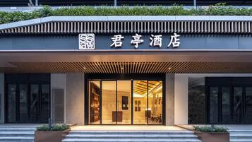 Entrada de hotel com design moderno, destacando uma placa e interior bem iluminado visível pelas portas de vidro.
