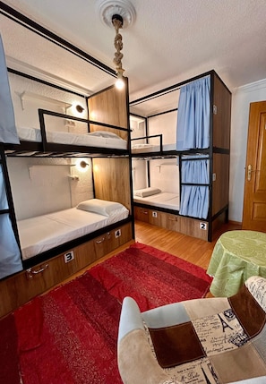 Quarto com beliches, tapete vermelho e uma pequena mesa com toalha verde.