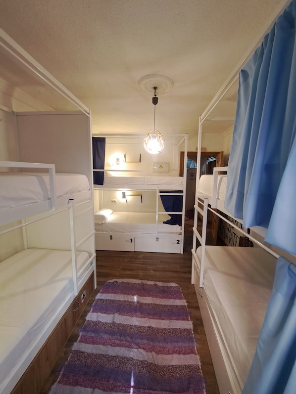 Quarto com beliche, piso de madeira, tapete listrado e luminária no teto.