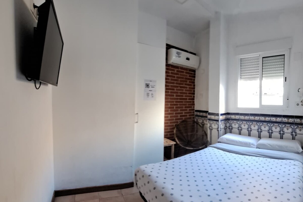Quarto com cama, televisão na parede, janela com persianas e ar condicionado.
