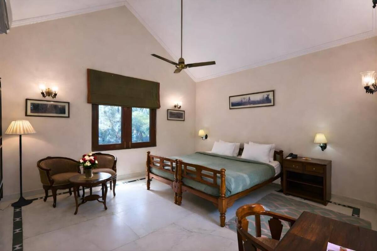 Quarto com cama, uma cadeira, mesa, abajur e ventilador de teto.