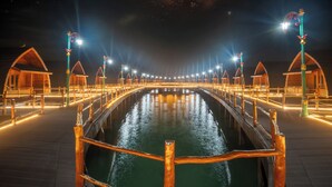 Vista noturna de um calçadão à beira-mar, com pavilhões de madeira e um corpo d'água refletindo.