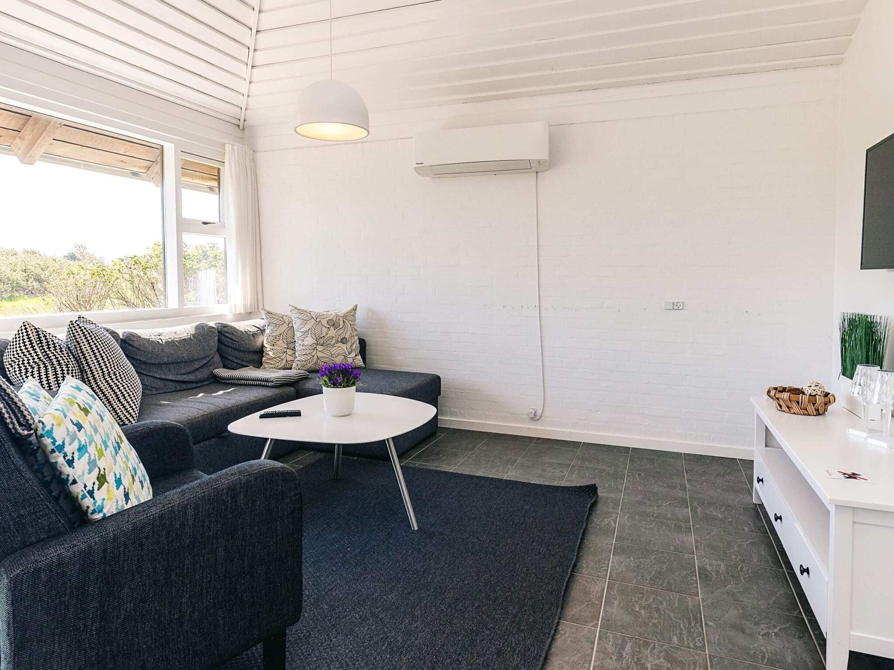 Uma sala de estar moderna com um sofá cinzento, uma mesa de centro redonda e uma parede branca com um aparelho de ar condicionado.