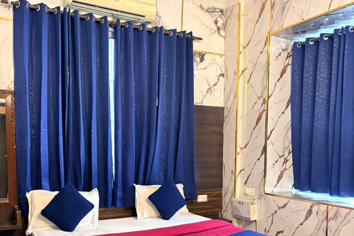 Quarto de hotel com parede em estilo marmore, cama com roupa de cama vermelha e azul, e cortinas azuis.