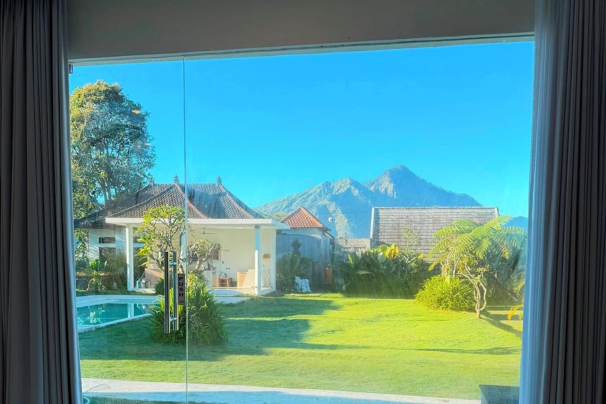 Um quarto com uma cama grande, vista para uma casa e uma montanha ao fundo.