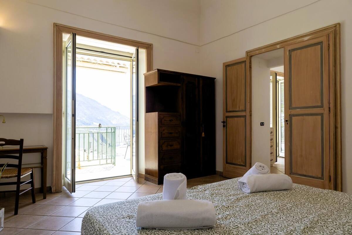 Quarto com cama, escrivaninha e guarda-roupa. Possui varanda com vista para as montanhas.