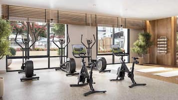 Uma academia com bicicletas ergométricas, um banco de musculação e uma grande janela com vista para o exterior.