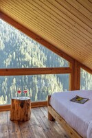 Quarto com uma janela grande, uma cama de madeira e uma mesa pequena com duas taças de vinho tinto.
