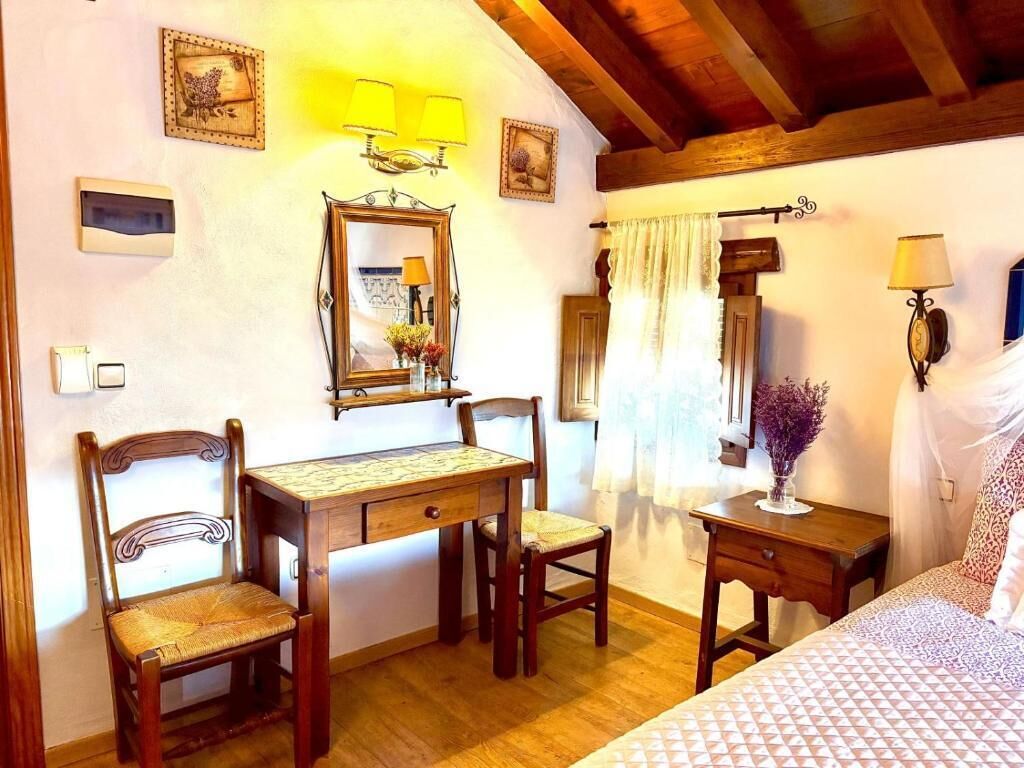 Quarto com escrivaninha de madeira, duas cadeiras, uma cama e um espelho.