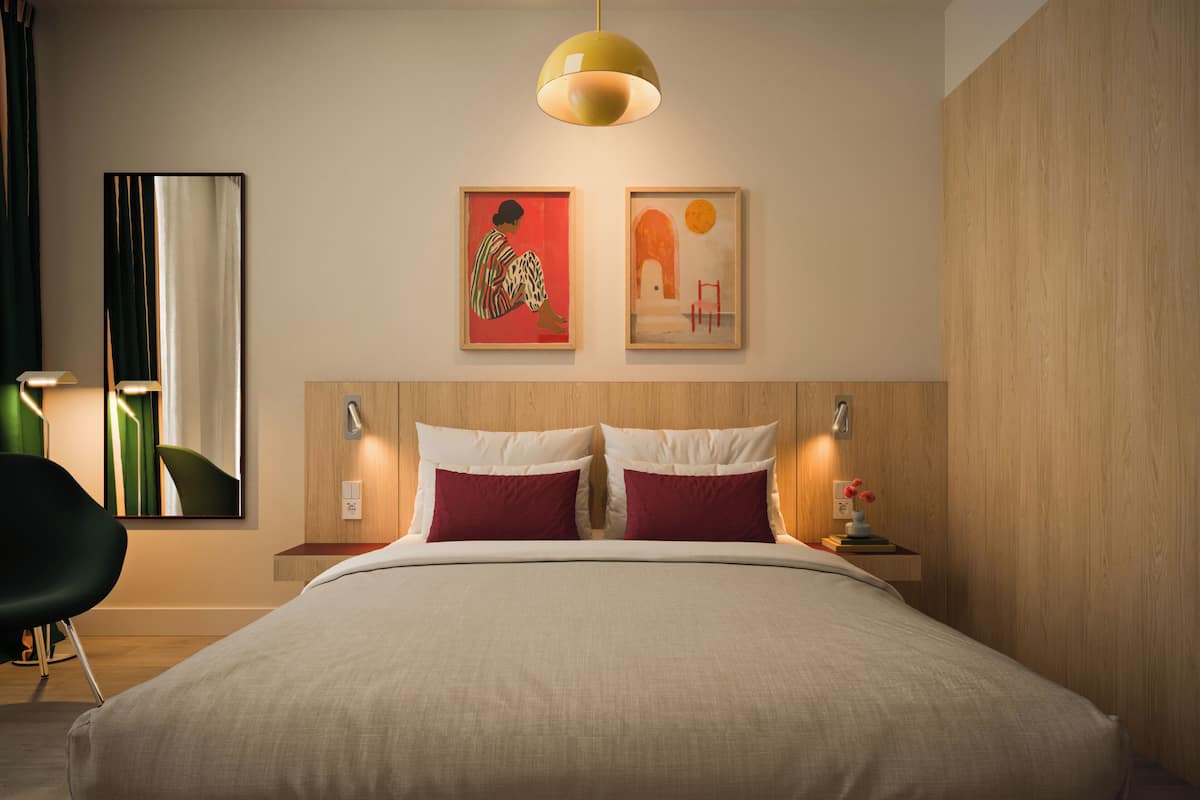 Quarto de hotel moderno com uma cama grande, duas mesas de cabeceira, um criado-mudo, uma cadeira e obras de arte na parede.