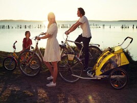 Uma família com bicicletas e um triciclo à beira de um lago.