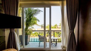 Quarto com uma grande porta de vidro deslizante que dá para uma varanda com piscina, móveis de exterior e uma palmeira.