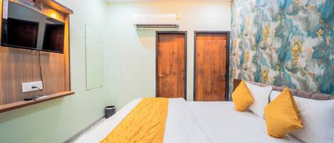 Quarto de hotel com cama, televisão, aparelho de ar condicionado e parede com padrão decorativo.