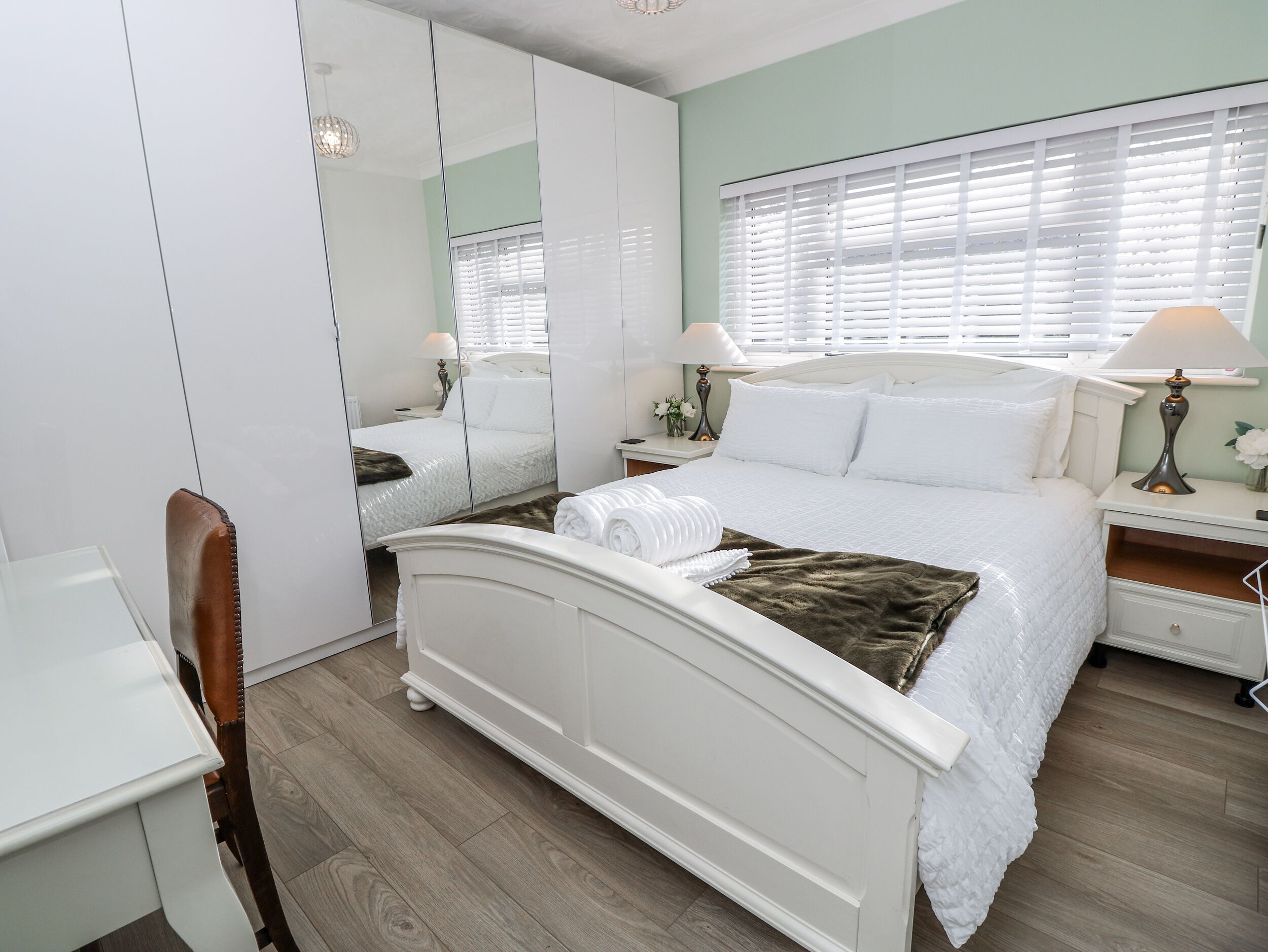 Quarto bem arrumado com cama, mesas de cabeceira, espelho e escrivaninha.