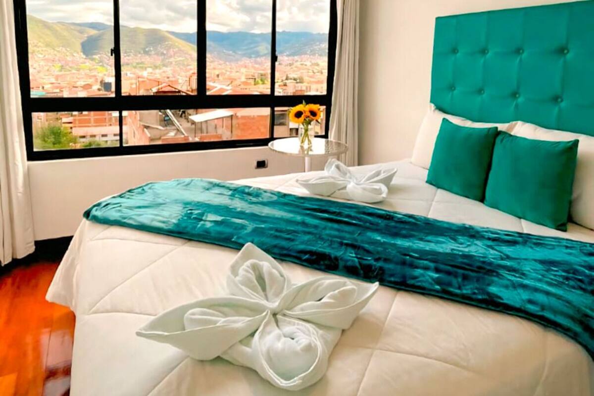 Quarto de hotel com cama, vista para a cidade através de grandes janelas e cabeceira verde.