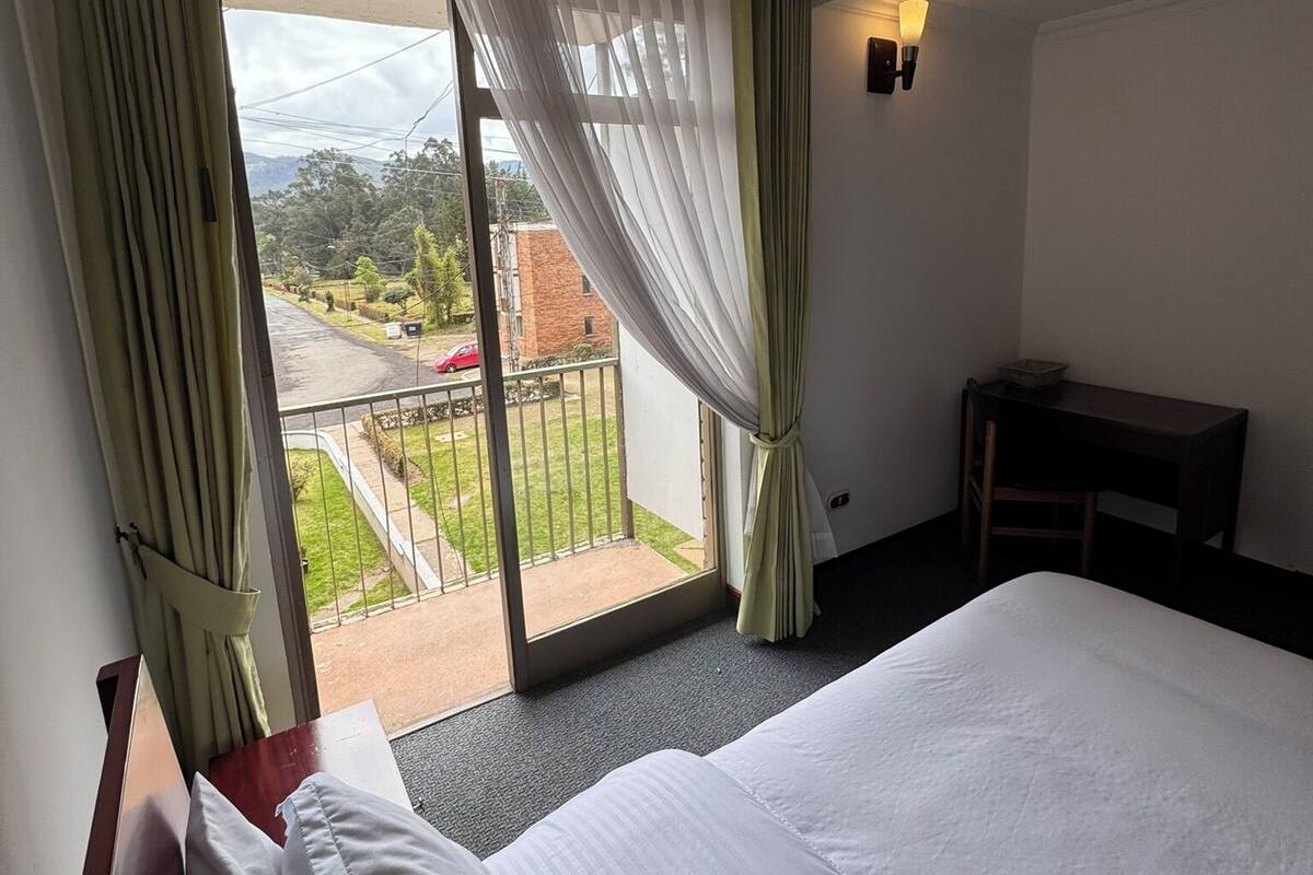 Quarto de hotel com uma cama, uma mesa e vista para o exterior.
