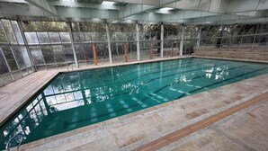 Piscina interior com água cristalina, cercada por paredes de vidro e chão revestido com azulejos.