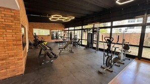 Uma academia com diversos equipamentos de exercício, grandes janelas e uma parede de tijolos.