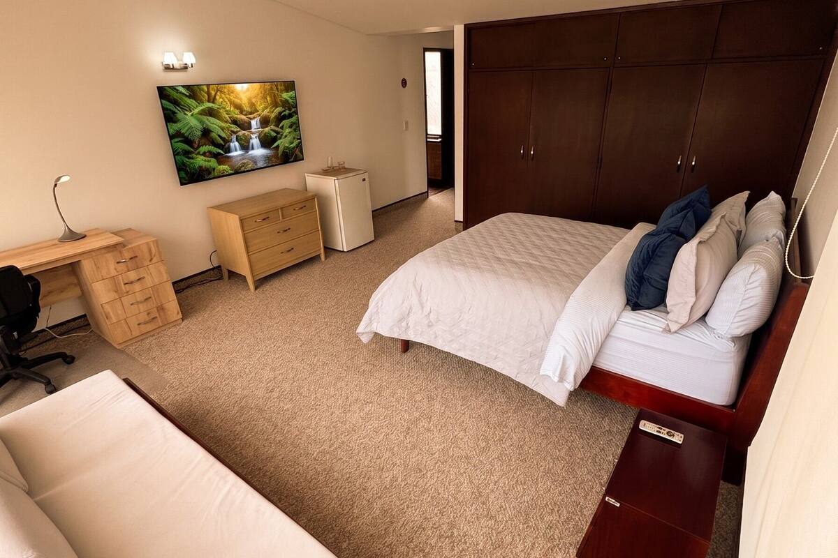 Quarto com cama, escrivaninha, cômoda, televisão e guarda-roupa.