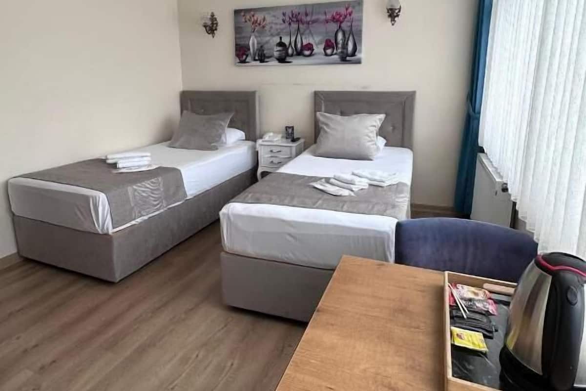 Quarto de hotel com duas camas, uma mesa de madeira, cafeteira e um quadro na parede.