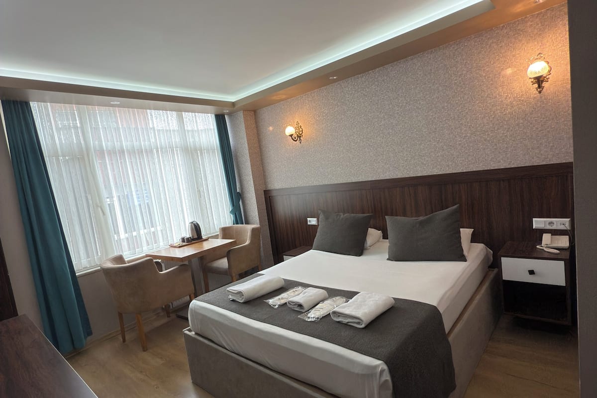 Quarto de hotel moderno com uma cama grande, mesas de cabeceira, uma escrivaninha e uma janela com cortinas.
