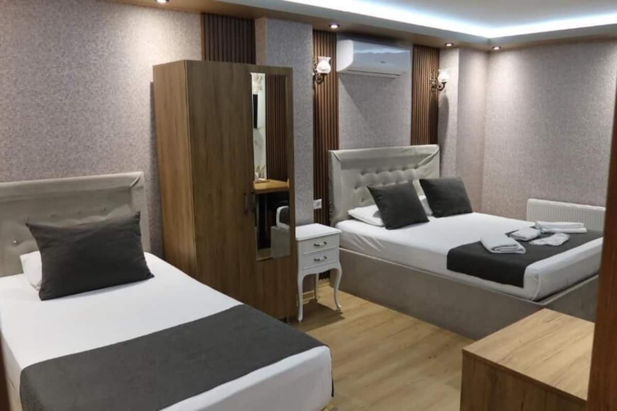 Quarto de hotel com duas camas, um guarda-roupa de madeira, uma escrivaninha pequena e um espelho.