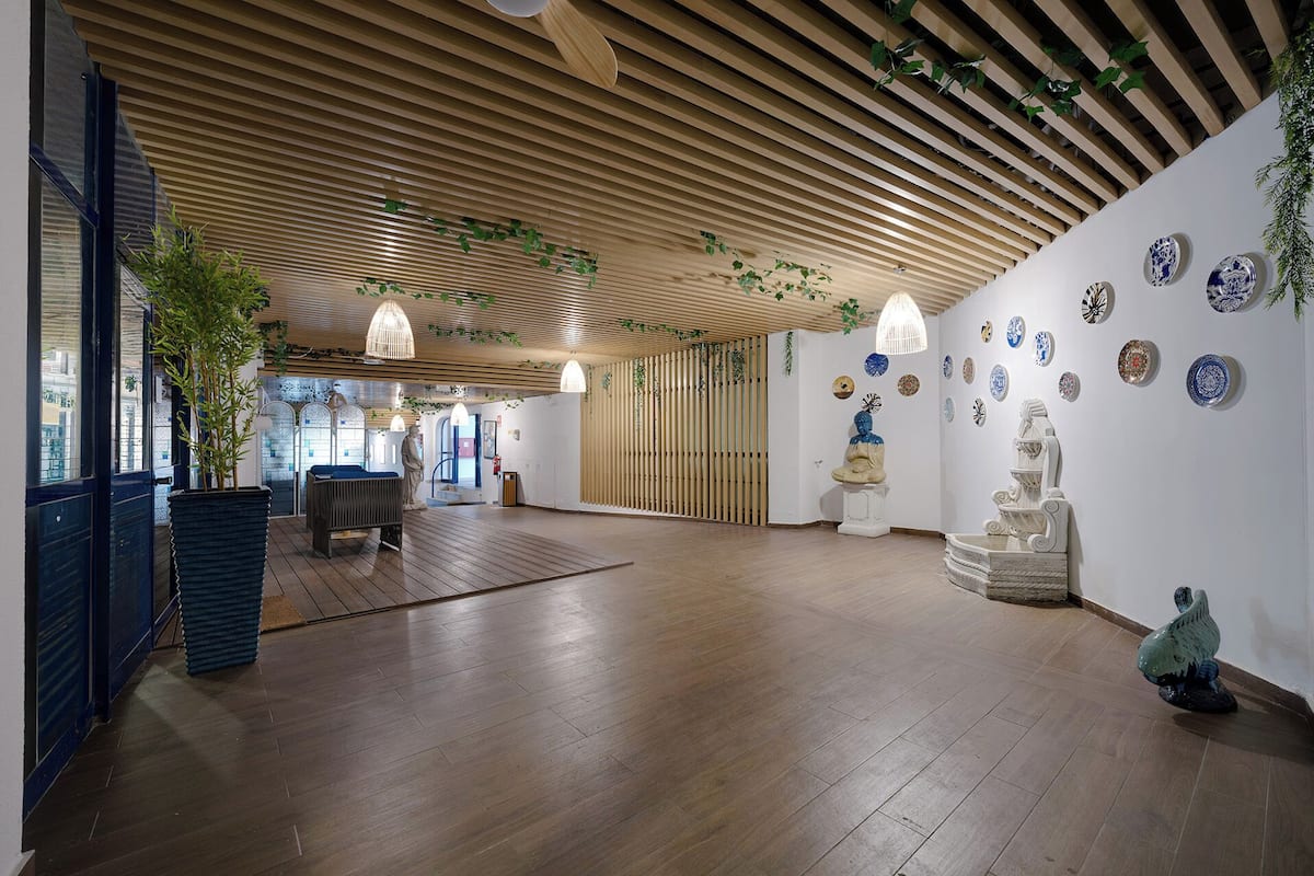 Um hall amplo com piso de madeira, uma grande planta em vaso e diversas placas decorativas nas paredes.