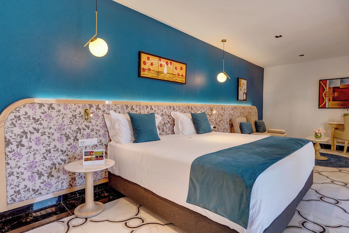 Quarto de hotel com uma cama grande, papel de parede floral e uma parede azul decorativa.