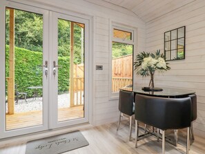Quarto com porta de correr de vidro que dá para um pátio externo, uma mesa pequena com duas cadeiras e um vaso com flores na parede.