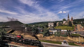 Uma estação de trem com uma locomotiva a vapor, uma igreja com uma torre alta e uma ponte ao fundo.