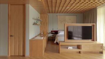 Quarto de hotel moderno com teto de madeira, cama com roupa de cama branca, televisão em suporte de madeira e uma pequena escrivaninha de madeira com cadeira.